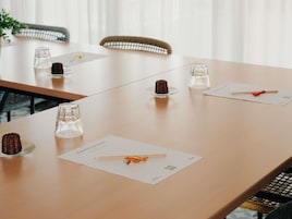 Mesa de conferência com documentos, uma caneta e uma sobremesa de chocolate pequena.