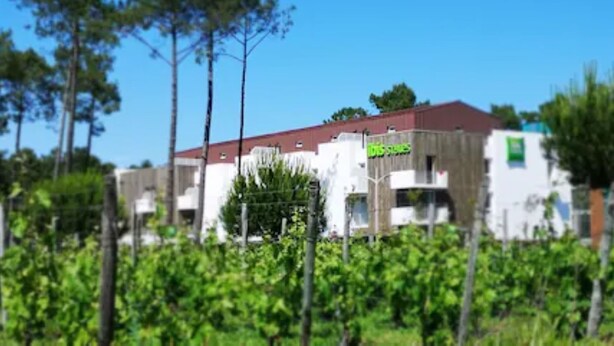 Edifício com telhado vermelho e paredes brancas, rodeado por vegetação.
