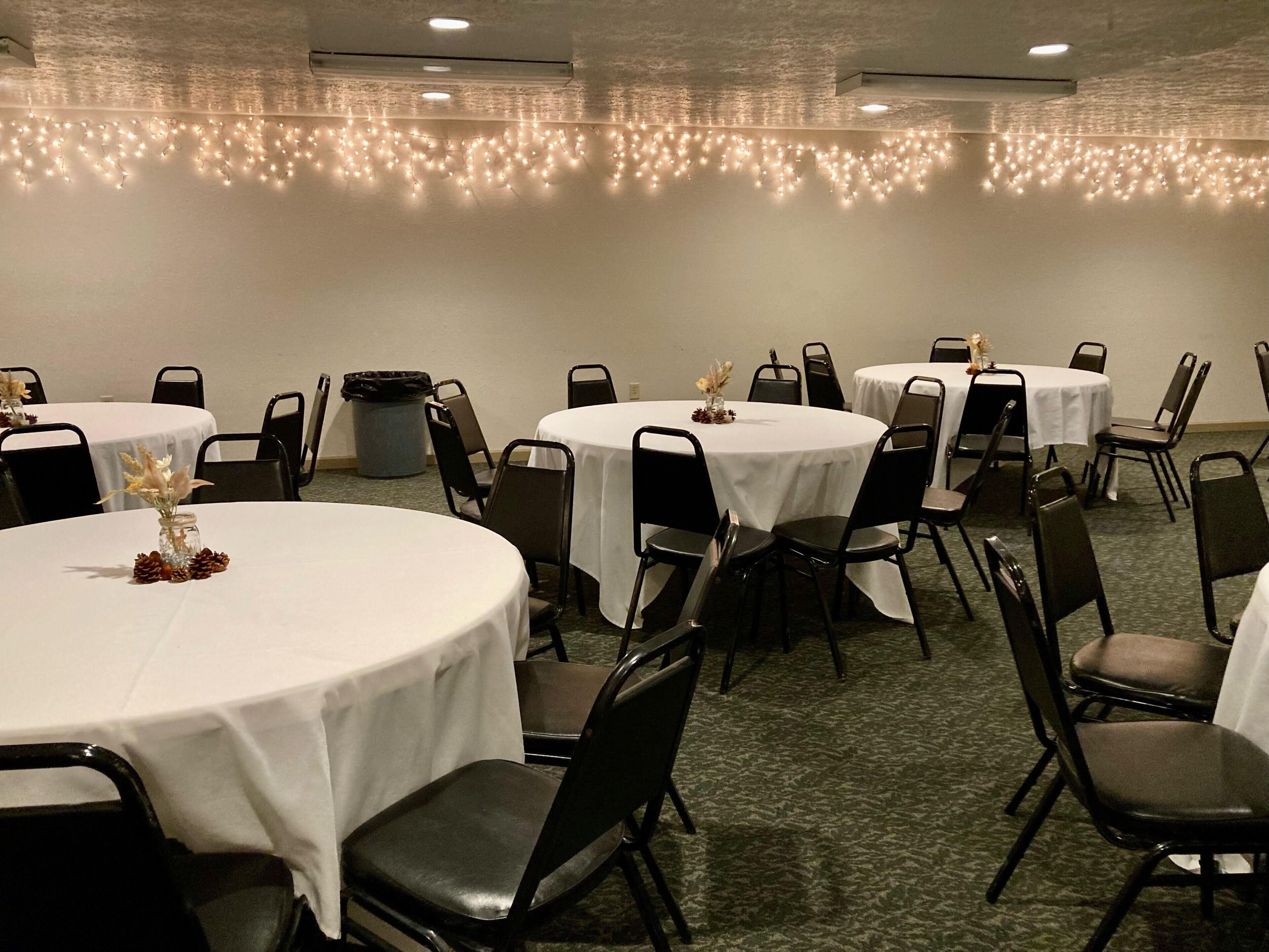 Uma sala de conferências com mesas redondas, cadeiras pretas, toalhas de mesa brancas e uma guirlanda decorativa no teto.