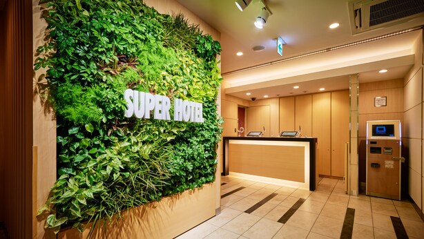 Uma área de recepção com parede verde, balcão de atendimento e uma tela digital.