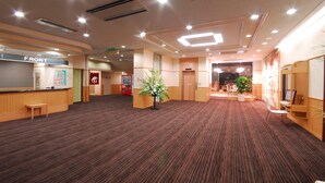 A spacious lobby with a reception desk labeled "FRONT," a vending machine, and a potted plant.