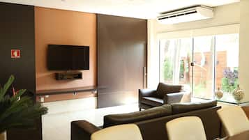 Uma área de espera moderna com televisão de tela plana na parede, assentos de couro e uma grande janela com vista para o exterior.