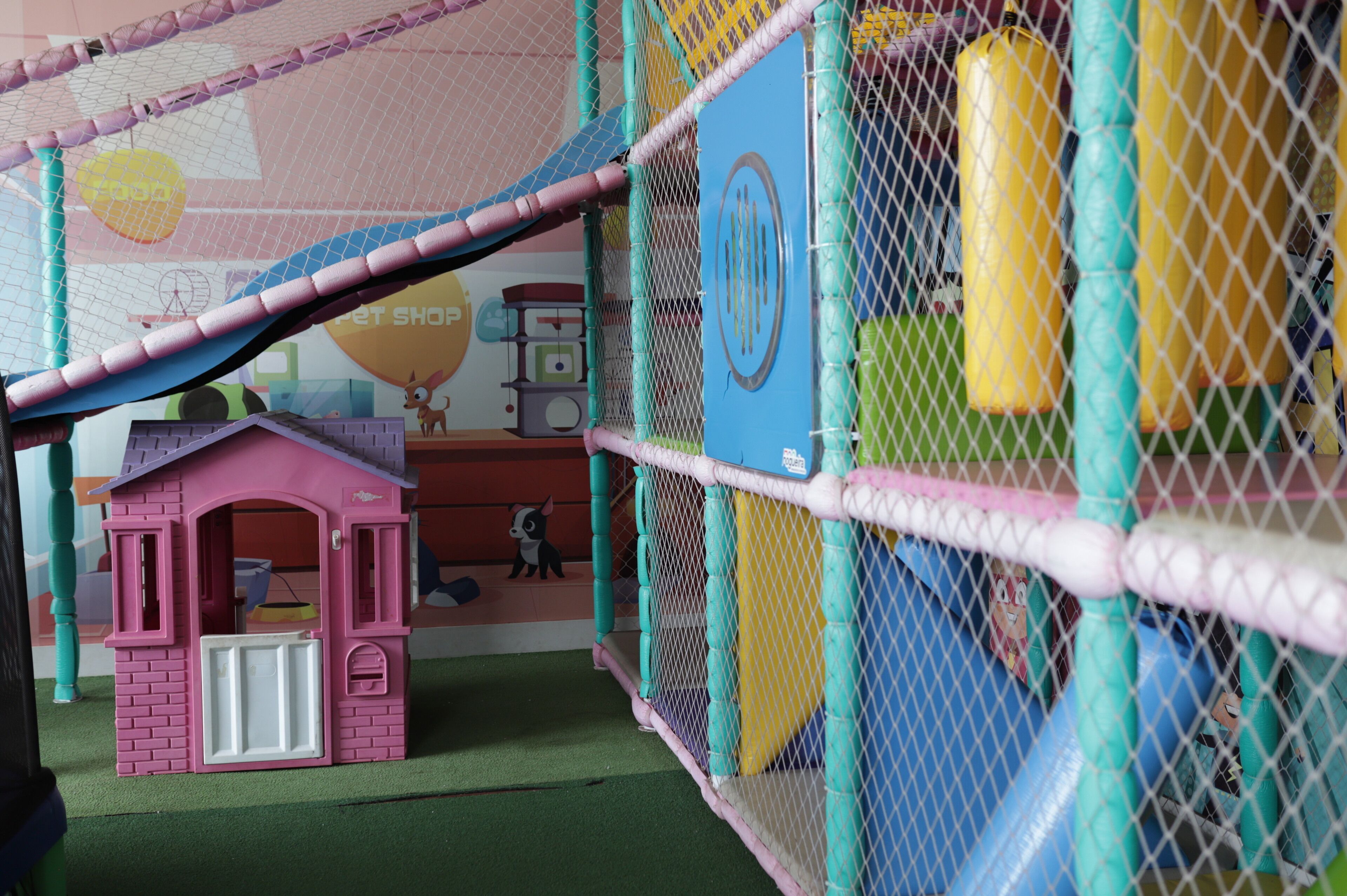 Uma área de recreação infantil com uma casinha rosa, um escorrega e um espaço cercado por rede.