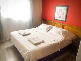 Uma cama bem arrumada com lençóis e almofadas brancos, uma cabeceira de madeira e uma obra de arte emoldurada na parede.