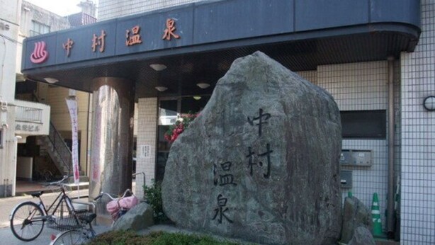 Entrada de um edifício com uma rocha grande gravada com caracteres chineses, uma bicicleta estacionada perto e uma placa sobre a entrada.
