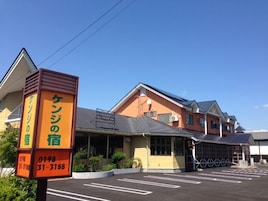 Hotel com estacionamento, placa com informações de contato e edifício com telhado inclinado.