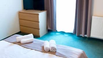 Quarto de hotel com uma cama, uma televisão sobre uma cômoda de madeira e uma janela com cortinas.