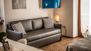 Uma sala de estar moderna com um sofá de couro, uma TV de tela plana, uma mesinha lateral e um abajur.