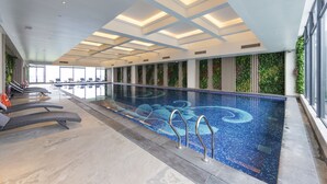 Piscina interior moderna com chão em azulejo, espreguiçadeiras e teto com iluminação embutida.
