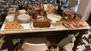 Uma mesa de jantar com diversos alimentos e utensílios, rodeada de cadeiras.