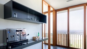 Uma cozinha moderna com máquina de café expresso embutida, uma prateleira preta acima e uma varanda com vista.