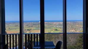 Uma varanda com vista para uma paisagem costeira, incluindo campos e uma cidade distante.