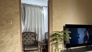 Uma sala de estar com poltrona estofada, planta em vaso, televisão e piso de madeira.
