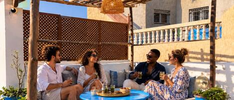 Um grupo de pessoas sentadas em um sofá azul sob uma pérgola de madeira, com uma mesa azul à frente.