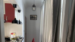 Uma cozinha pequena com bancada vermelha, um banquinho de madeira e um lustre.