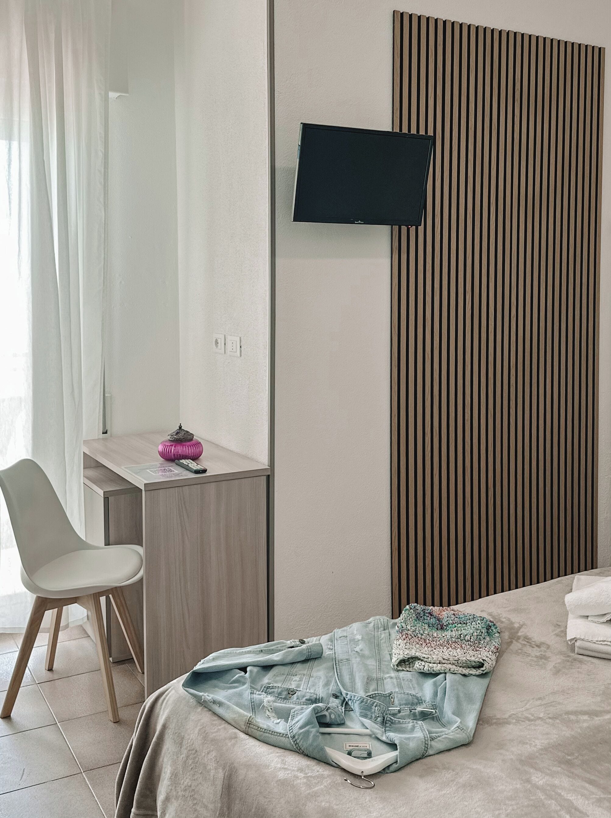 Quarto moderno com cama, escrivaninha, cadeira e televisão fixada na parede.