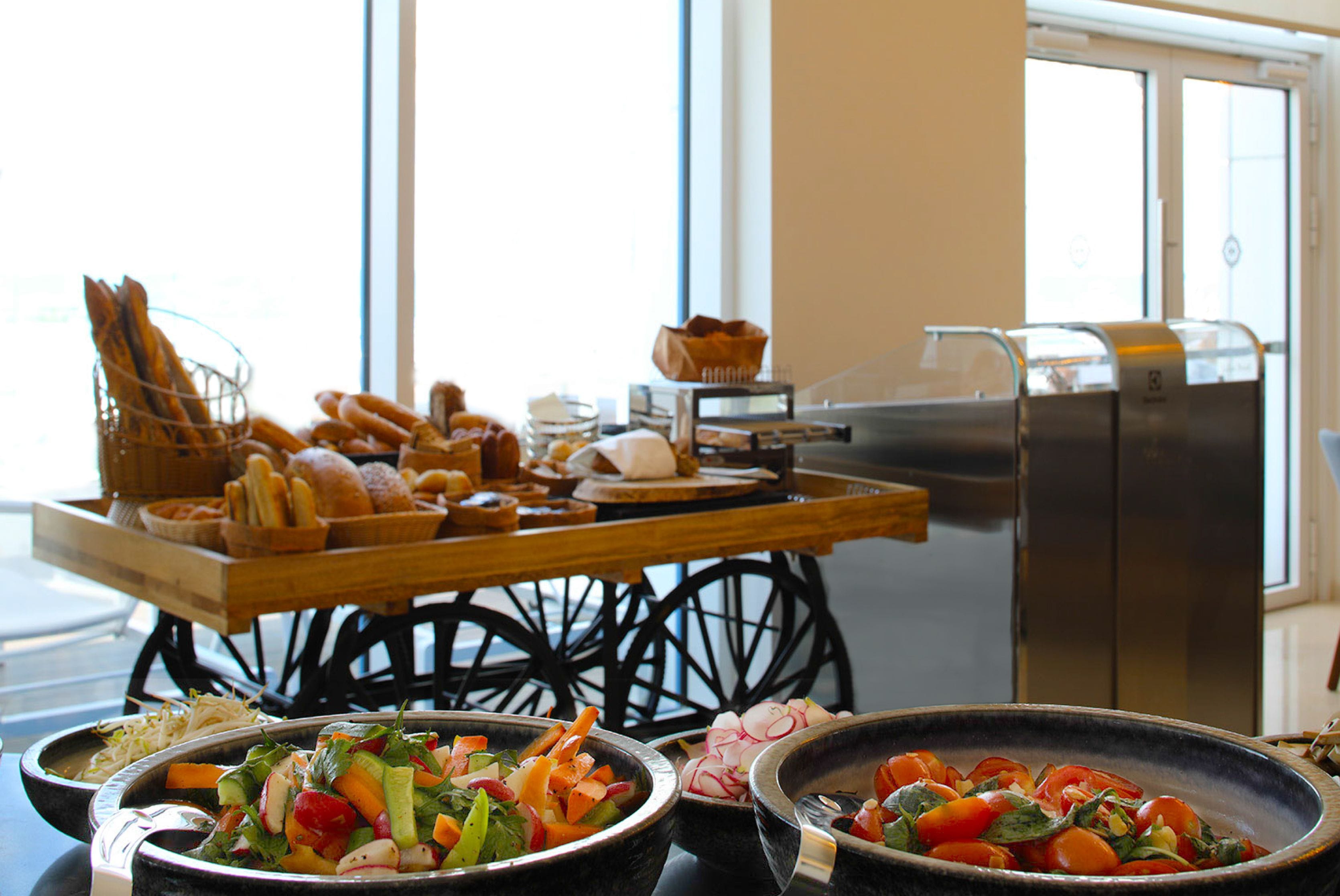 Uma mesa de buffet com diversos alimentos, incluindo saladas, legumes e pães.