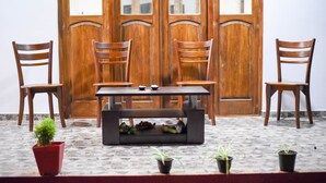 Uma área de refeições com mesa e cadeiras de madeira, um pequeno banco e plantas em vasos.