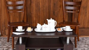 Uma mesa de madeira posta com xícaras de chá brancas, um bule, cubos de açúcar e biscoitos.