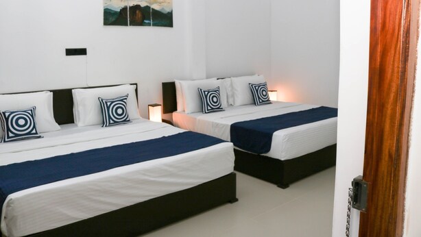 Duas camas de solteiro com roupa de cama branca e azul, um quadro na parede e uma porta de madeira.