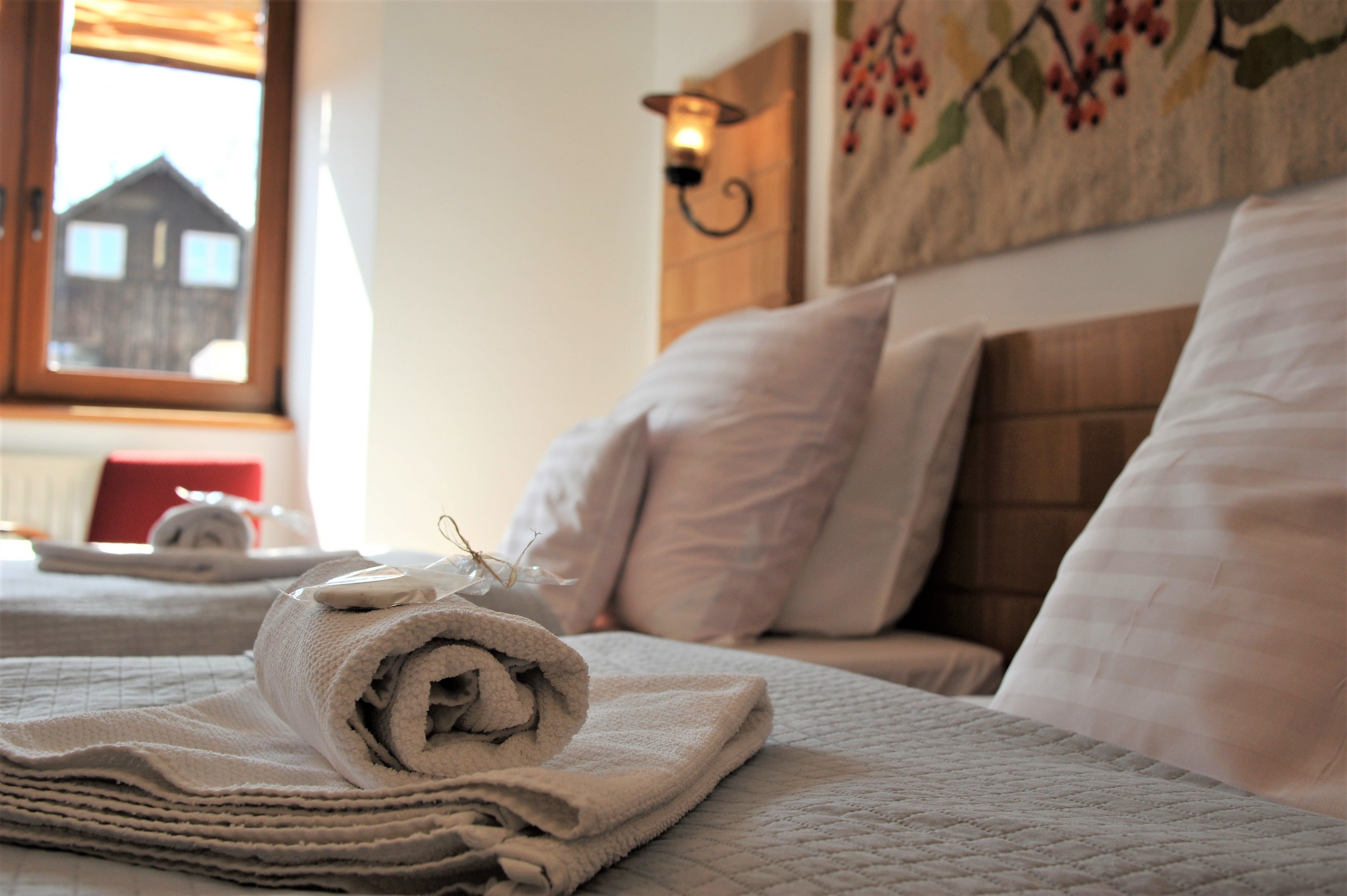 Cama bem arrumada com uma toalha branca enrolada e outra toalha branca dobrada.