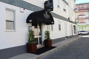 Hotel Vila Esteves, com toldo preto, duas plantas em vasos e rua de calçada.