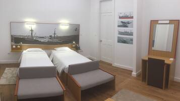 Quarto com duas camas de solteiro, uma escrivaninha de madeira, um espelho e uma grande moldura com a imagem de um navio.