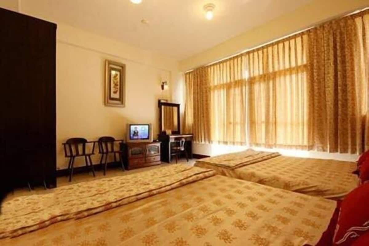 Quarto de hotel com duas camas, uma escrivaninha, uma cadeira, uma televisão e uma janela com cortinas.
