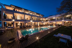 Um hotel moderno de vários andares com uma grande piscina ao ar livre, áreas de estar externas e um pátio bem iluminado.