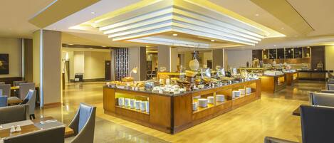 Um saguão de hotel moderno com uma área de buffet central, espaços de estar e piso polido.