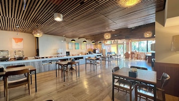Um café moderno com chão de madeira, um balcão comprido com diversos equipamentos e várias áreas de estar.
