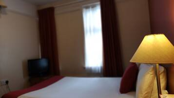 Quarto de hotel com uma cama, televisão, abajur e cortinas.