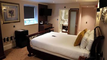 Quarto de hotel com cama, escrivaninha, televisão, janela com persianas, espelho e chuveiro.