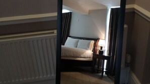 Quarto de hotel com uma cama, mesa de cabeceira, abajur e radiador.