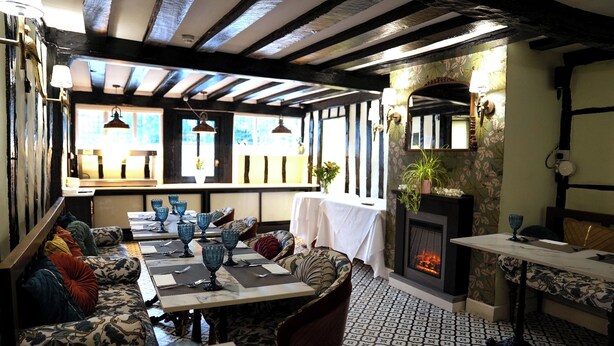 Um restaurante acolhedor com vigas de madeira, soalho estampado e lareira.