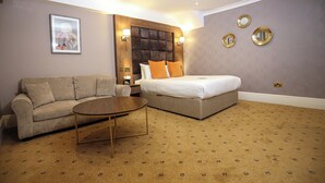 Quarto de hotel com cama, sofá, mesa de centro e um quadro na parede.