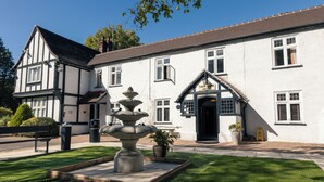 Hotel Tudor Lodge com uma fonte de pedra, um jardim bem cuidado e fachada de edifício tradicional.