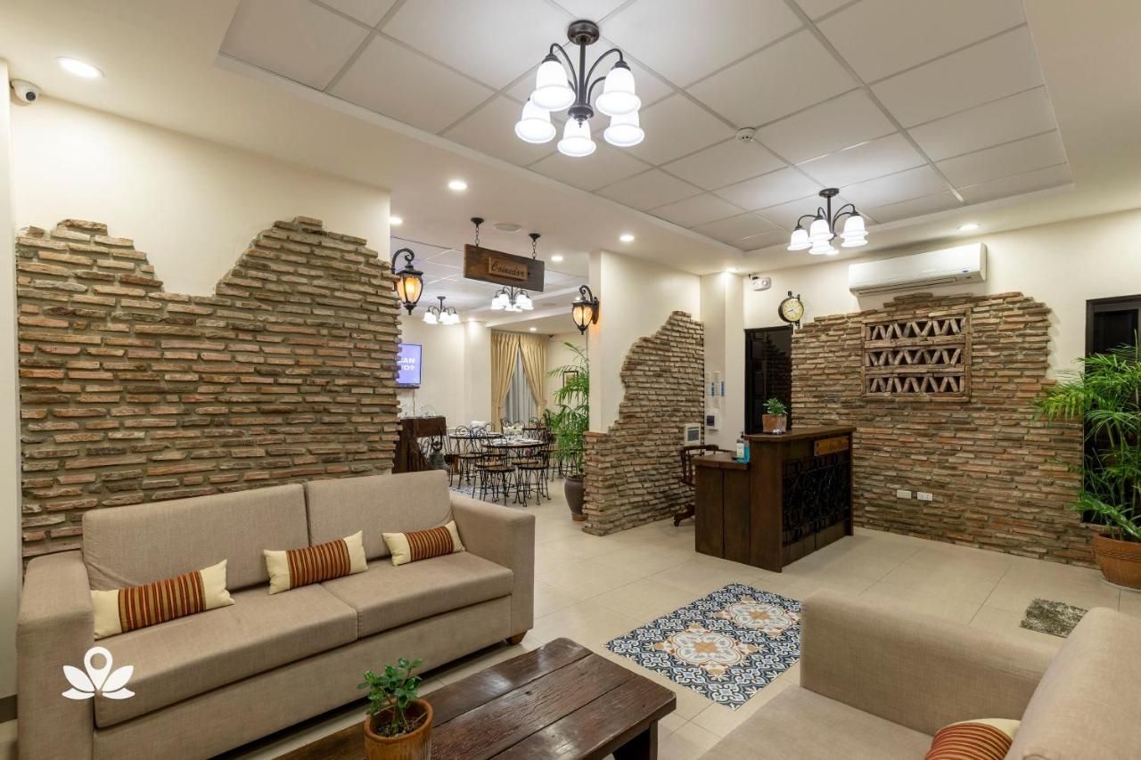 Sala de estar com sofá, mesa de centro e tapete estampado. Apresenta uma parede de pedra e um balcão de atendimento em madeira.