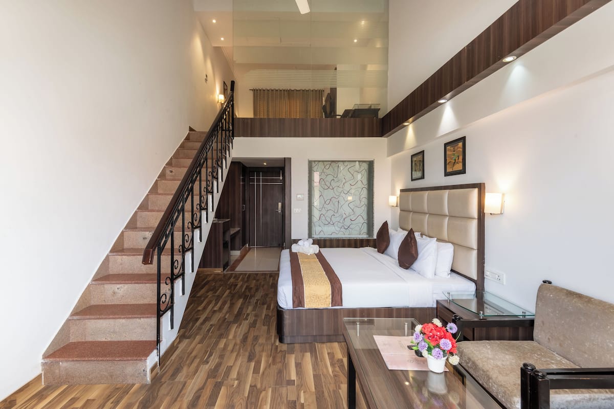 Quarto de hotel com cama, sofá, mesa de centro e escada.