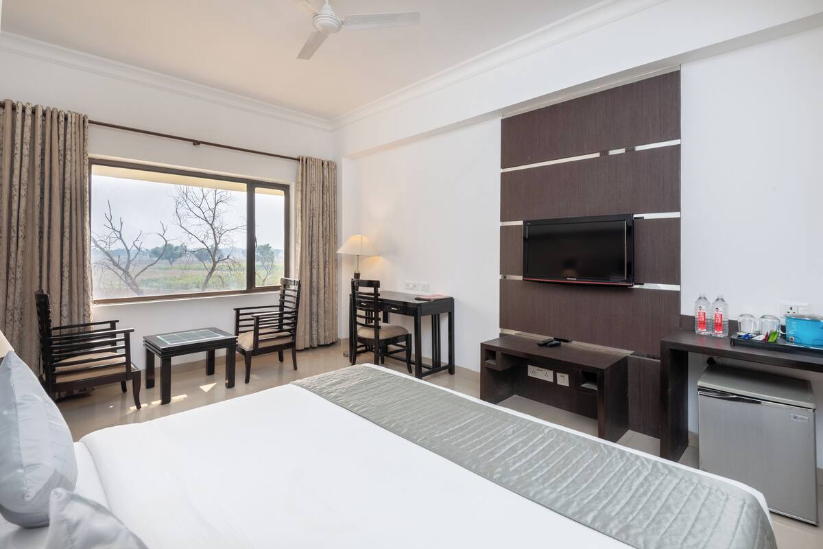 Quarto de hotel com uma cama grande, uma escrivaninha, uma cadeira, televisão fixada na parede e um pequeno frigorífico.
