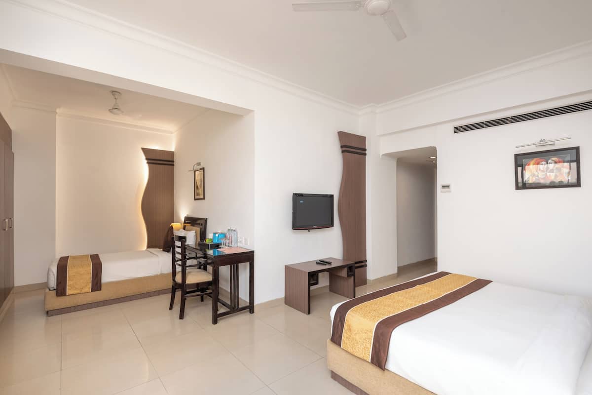 Quarto de hotel com cama, escrivaninha, cadeira, televisão e ventoinha no teto.