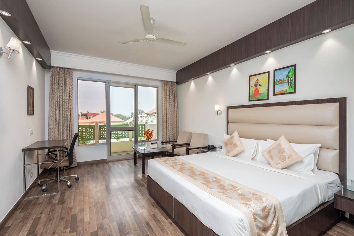 Quarto de hotel com uma cama grande, uma escrivaninha, uma cadeira e vista para o exterior.