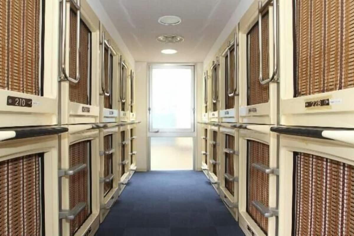 Um corredor com fileiras de quartos, cada um com uma placa de número, que leva a uma saída iluminada.