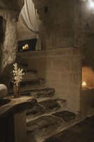 Uma escadaria de pedra com velas, um vaso com flores secas e uma parede rústica.