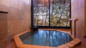 Uma banheira de hidromassagem com vista para árvores através de uma grande janela.