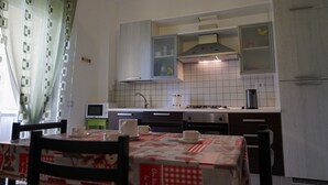 Cozinha moderna com micro-ondas, fogão e armários. Há uma mesa de jantar com cadeiras e uma janela com cortinas.
