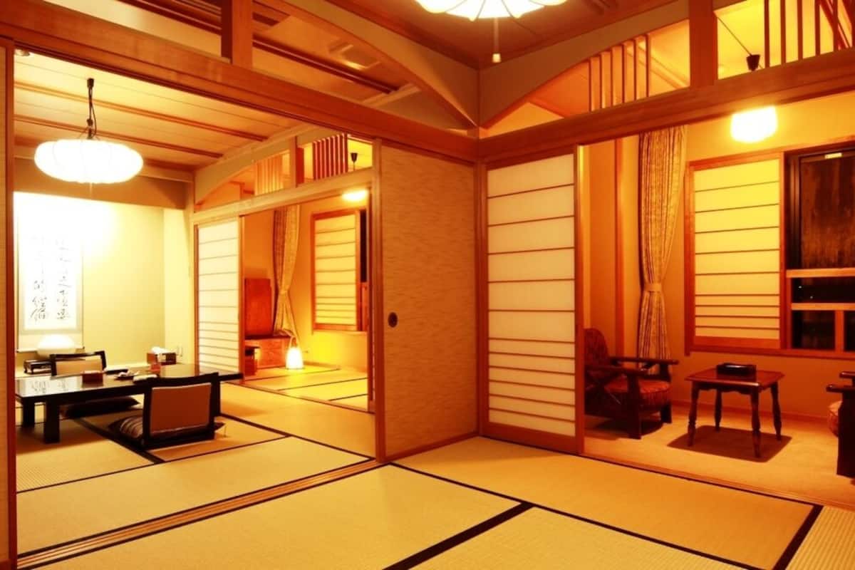 Um quarto japonês tradicional com tatames, portas deslizantes, uma mesa baixa com um assento e um candeeiro pendente.