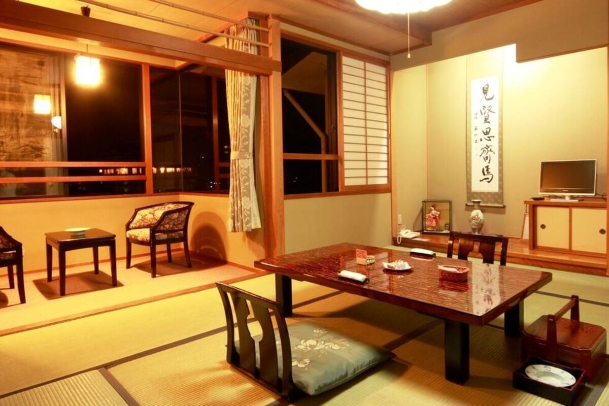 Um quarto japonês tradicional com tatames, uma mesa baixa com almofadas, televisão e portas deslizantes.