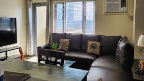 Uma sala de estar com sofá, mesa de centro, TV e ventilador de teto.