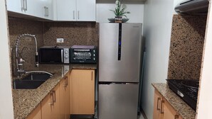 Cozinha compacta com armários brancos, geladeira de aço inoxidável, micro-ondas e pia.